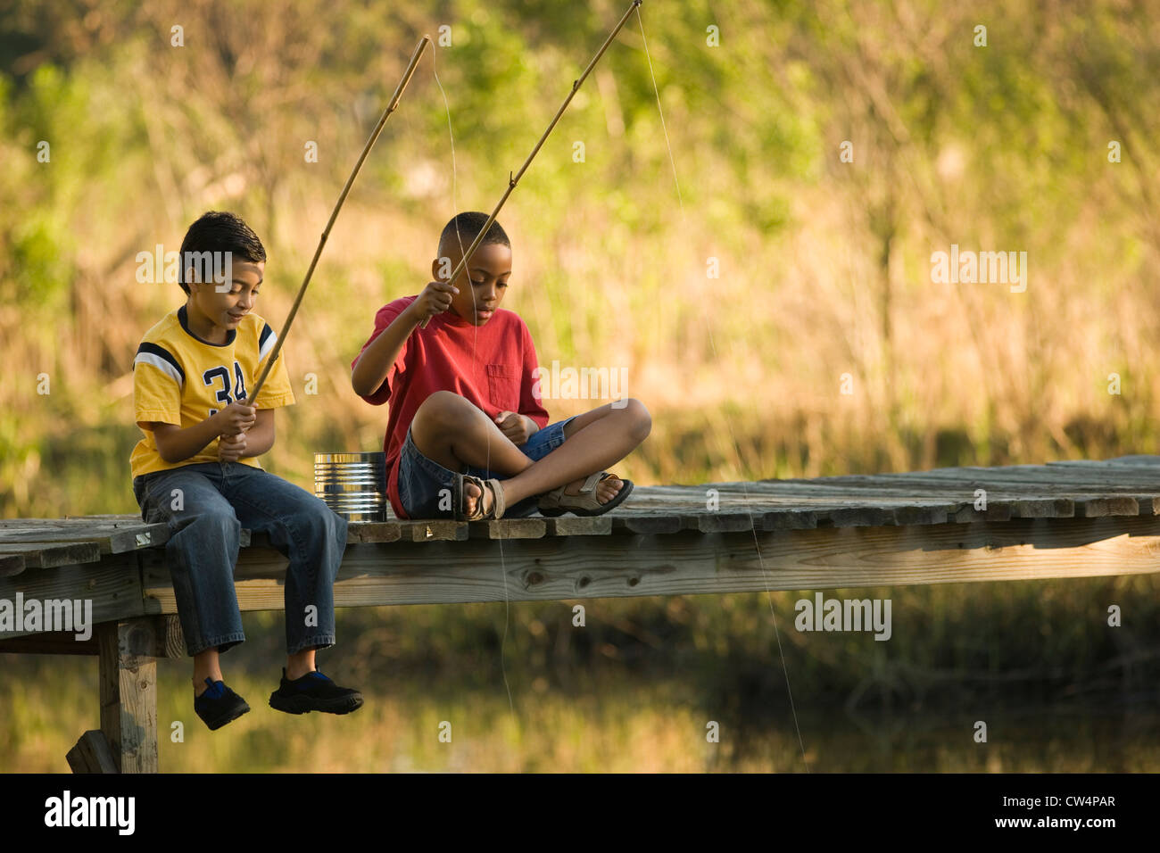 Friends fishing with fishing rods sitting on the jetty Stock Photo - Alamy
