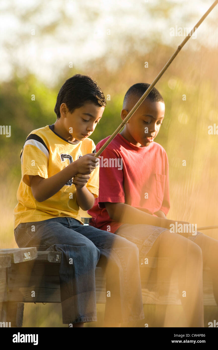 Friends fishing with fishing rods sitting on the jetty Stock Photo - Alamy