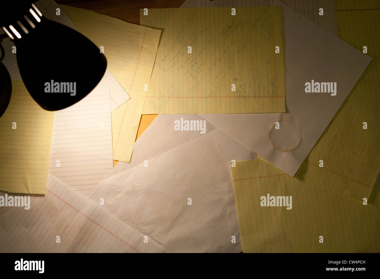A messy desktop covered in paper lit by a single desk lamp Stock Photo ...