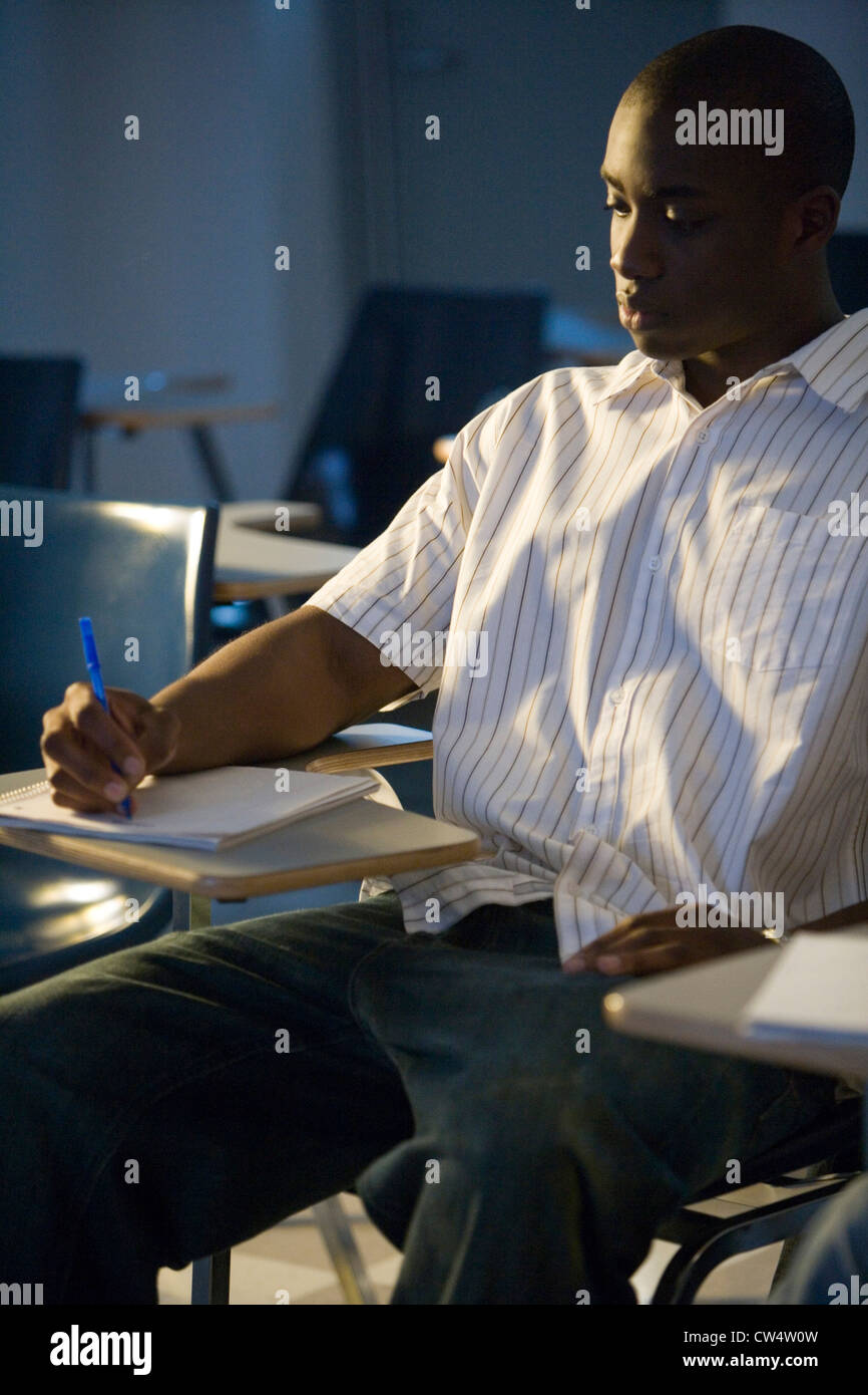 Male student writing on book in the classroom Stock Photo - Alamy