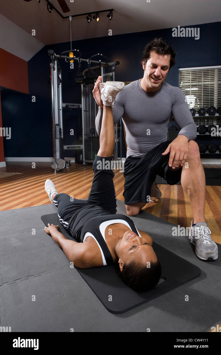 Trainer stretching leg of a young woman in the gym Stock Photo - Alamy