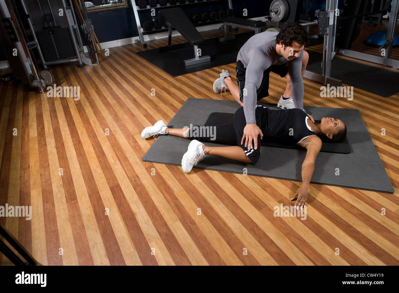 Trainer stretching leg of a young woman in the gym Stock Photo - Alamy