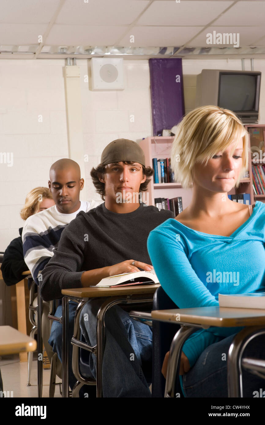 Portrait of student wearing cap while other students reading book in ...