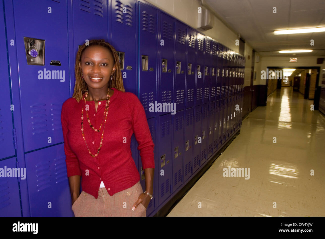 Portrait of a cheerful female teacher standing by locker in corridor ...