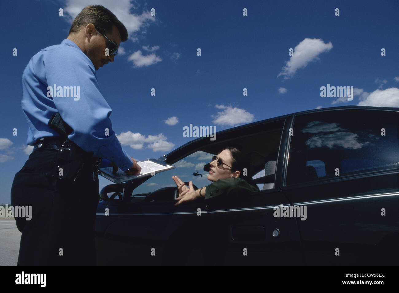 Police officer standing beside a car and writing a speeding ticket ...
