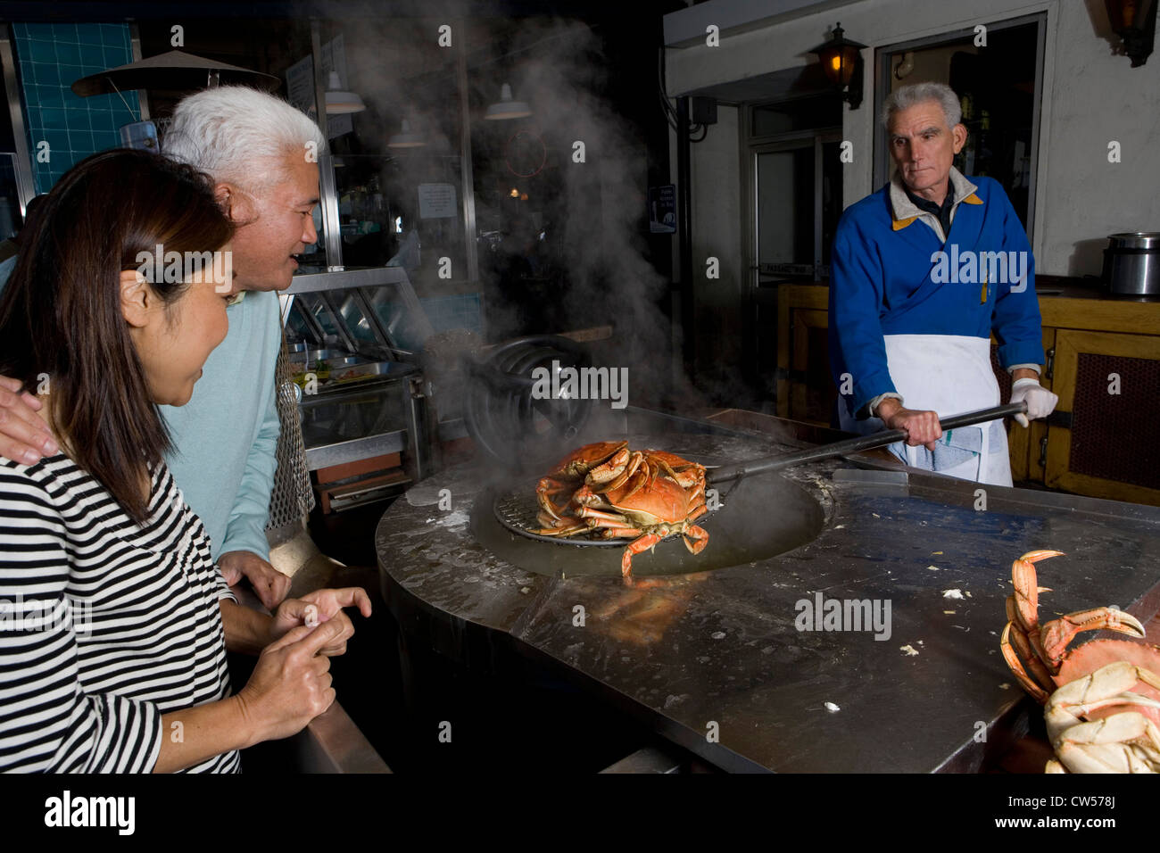 Mature couple standing and looking crabs being cooked by mature man in ...