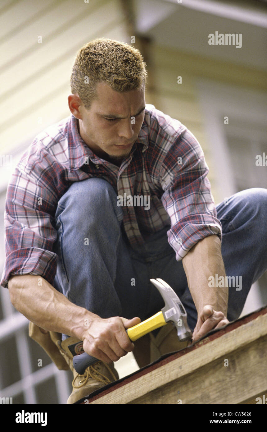 Young man hammering a nail into a wooden board Stock Photo - Alamy