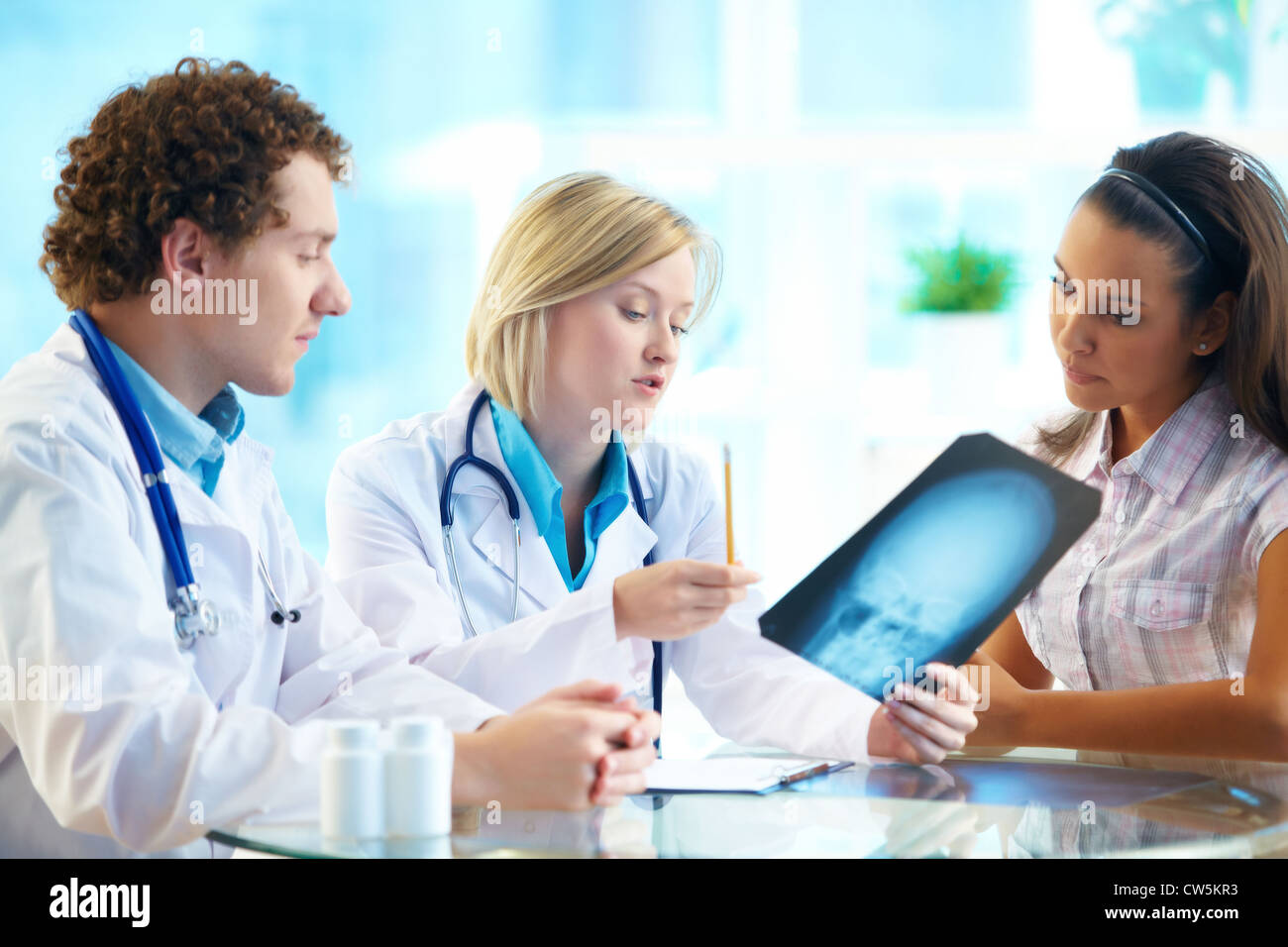 Portrait of two doctors and young female patient reading x-ray in ...
