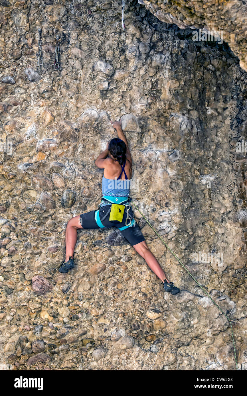 Woman high on a rock wall attempting to maneuver around an overhang ...
