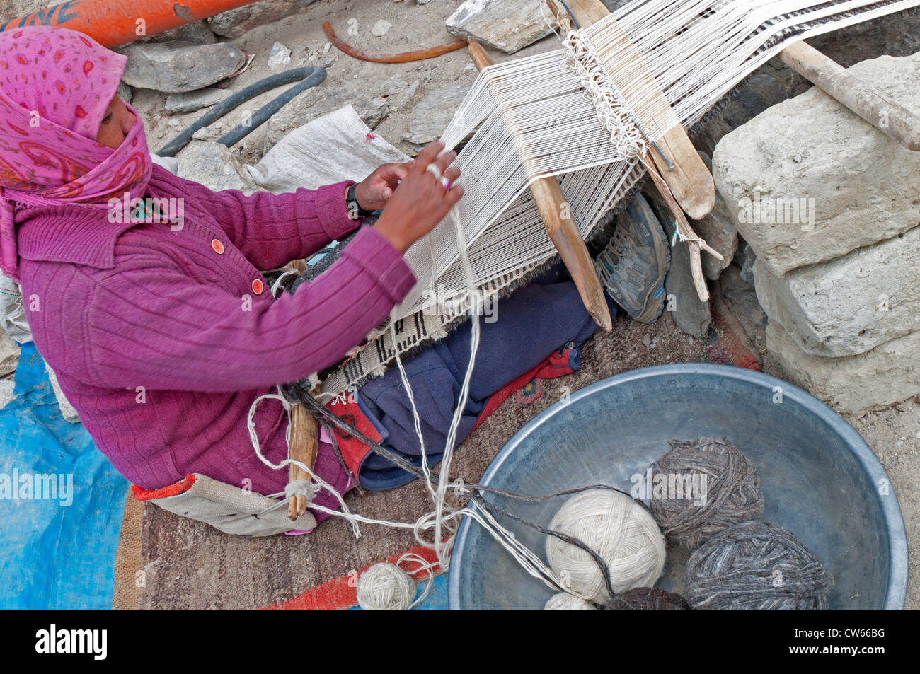 A nomad woman in a magenta sweater and scarf weaving on a loom at Kar ...