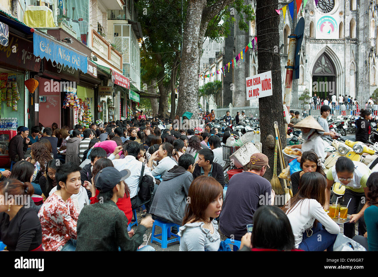 A crowd of people sitting in the streets front of an outdoor cafe with ...
