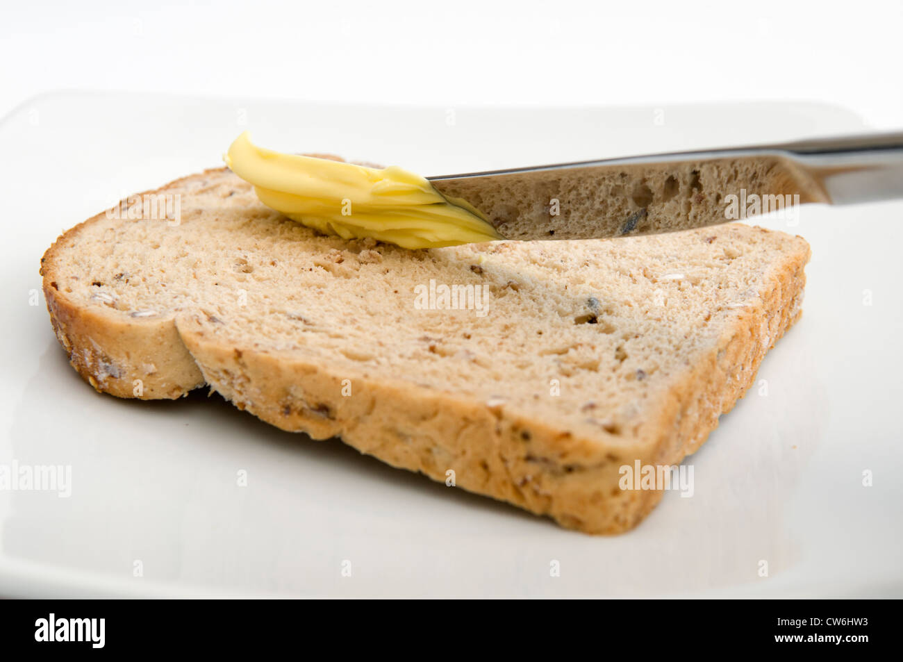 Slice of granary bread being buttered on white plate against white ...
