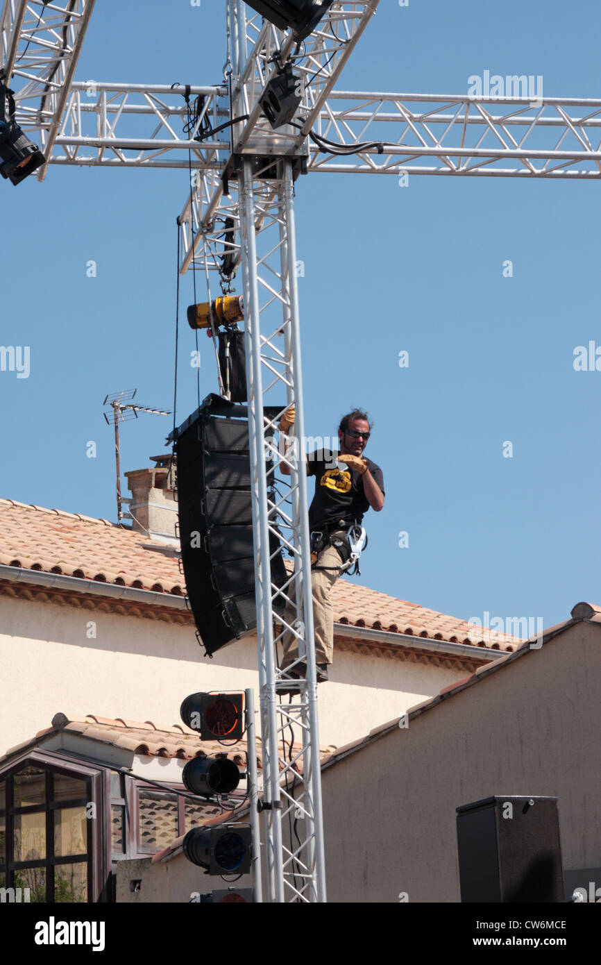 A sound engineer mounting a speaker above a temporary stage ready for a ...