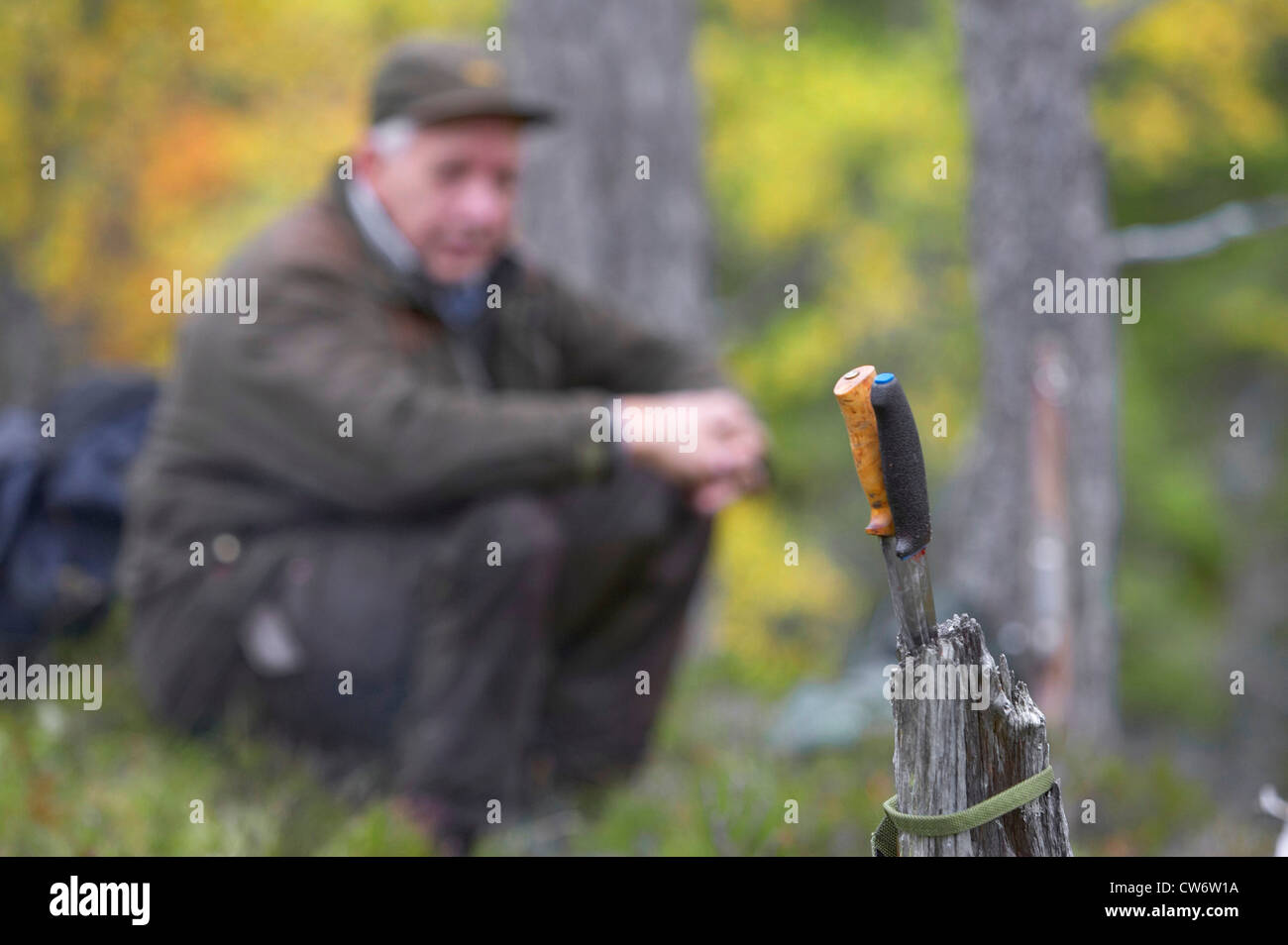 hunter sitting at a clearing during a break with two hunting knives ...