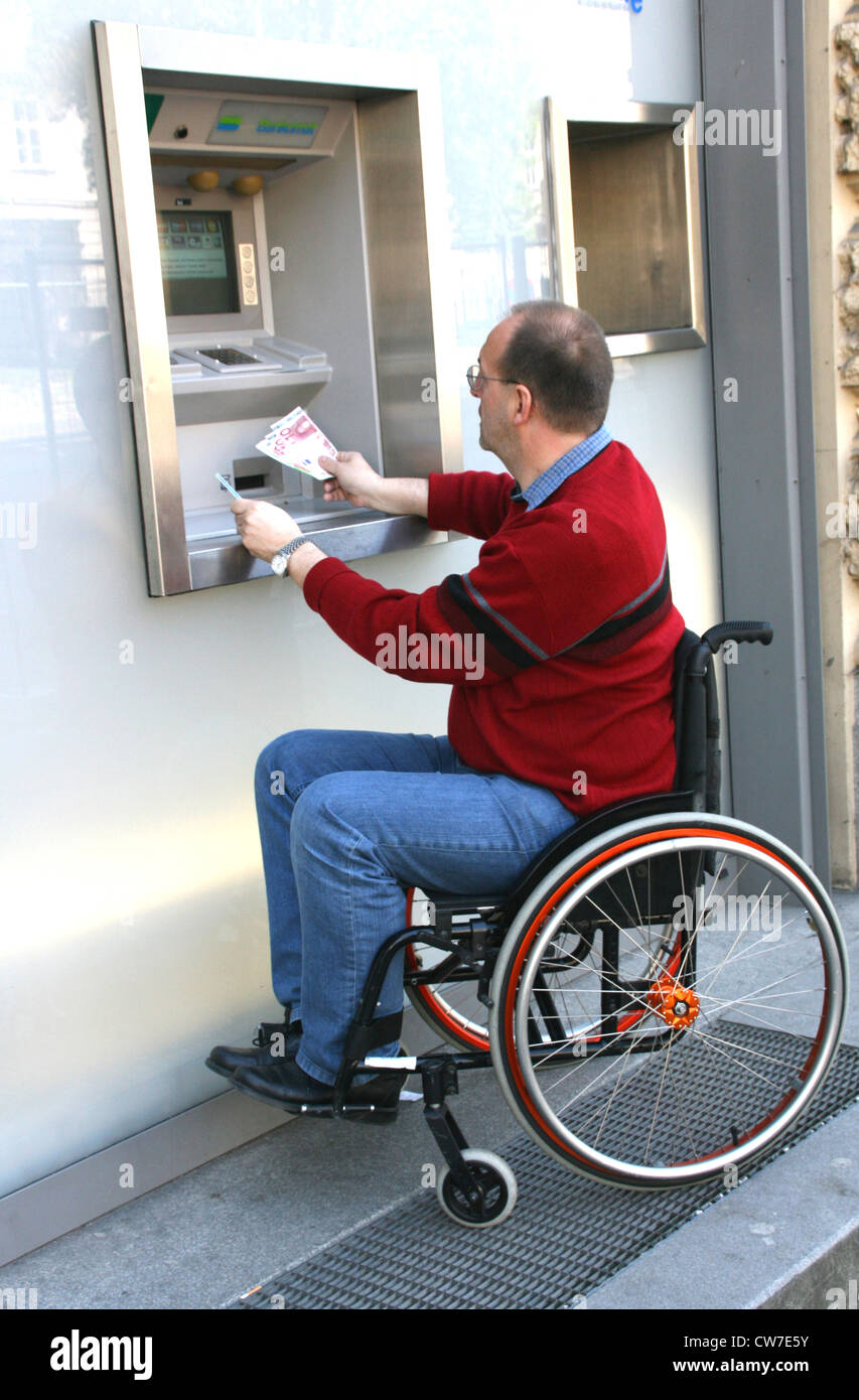 man in a wheel chair with euro bank notes at a automatic cash dispenser ...