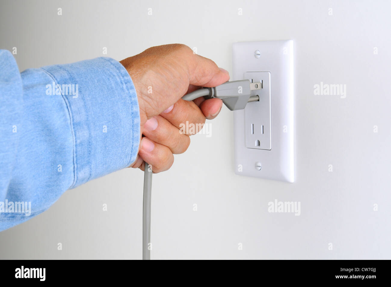 Closeup of a man's hand inserting an electrical plug into a wall socket ...