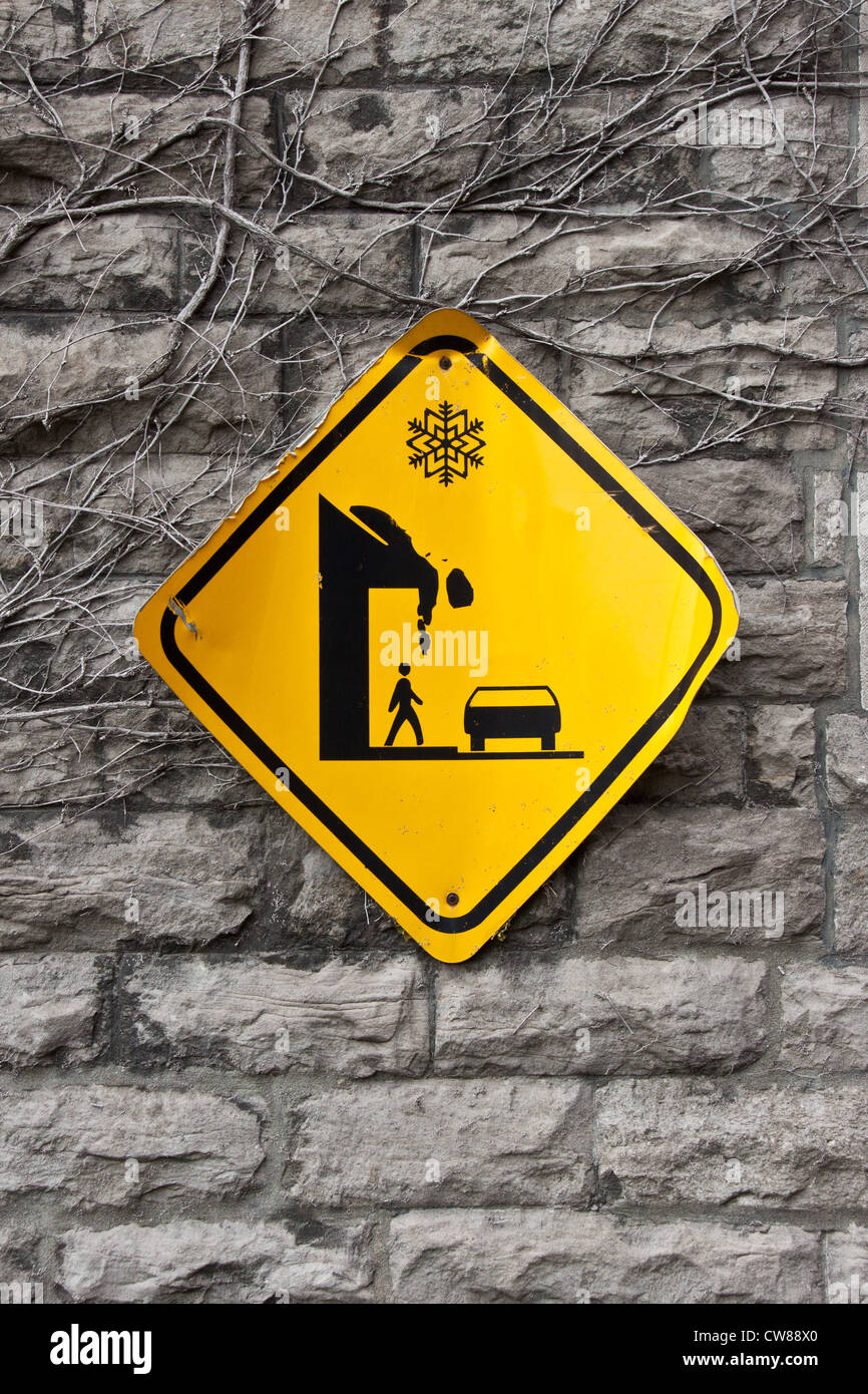 Yellow warning sigh about falling glass from the roof, on a stone wall ...
