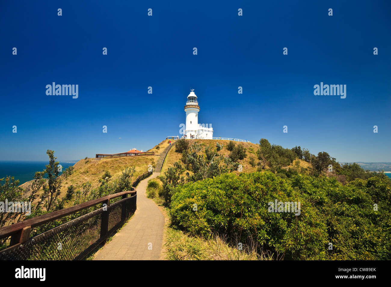 Landscape of rugged coastline path to pretty white lighthouse at Byron ...