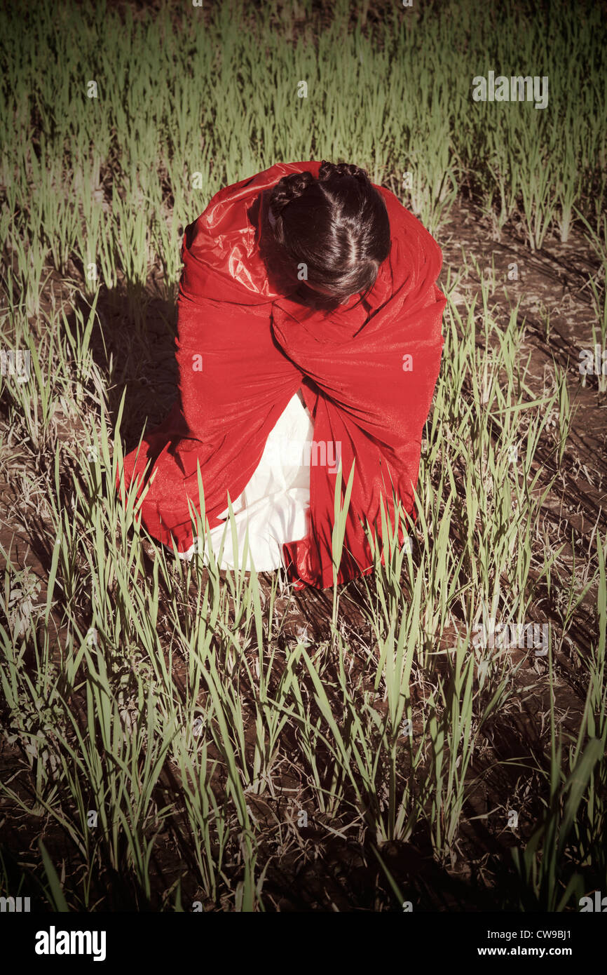 a woman in a red cloak crouching in a field Stock Photo - Alamy