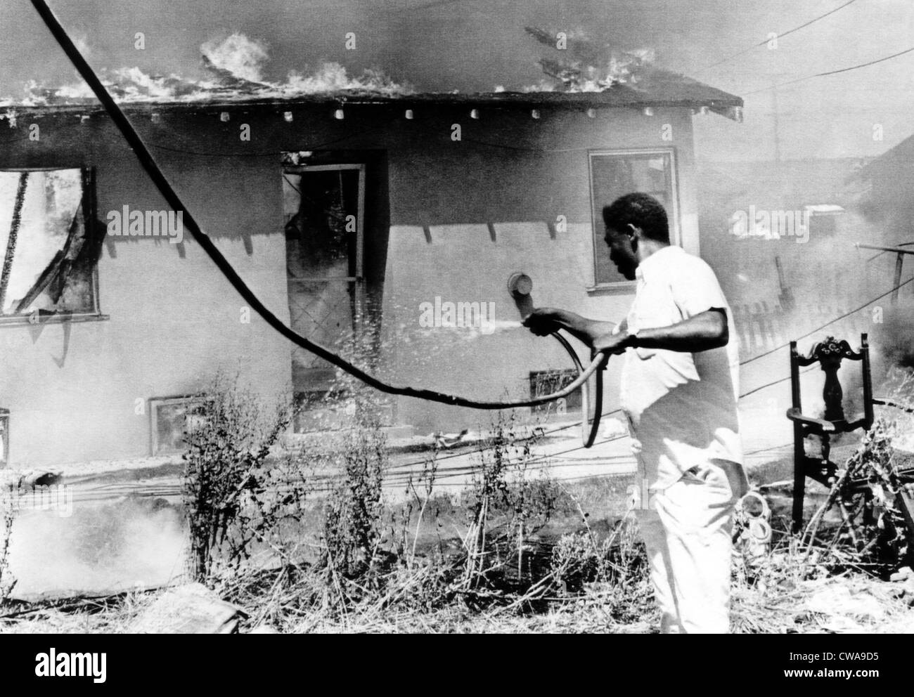 A man attempts to stop the fire destroying his home during the Watts ...