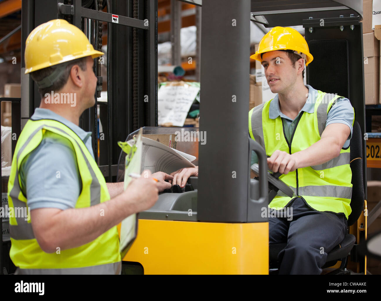 Two men in warehouse, one on forklift truck Stock Photo - Alamy
