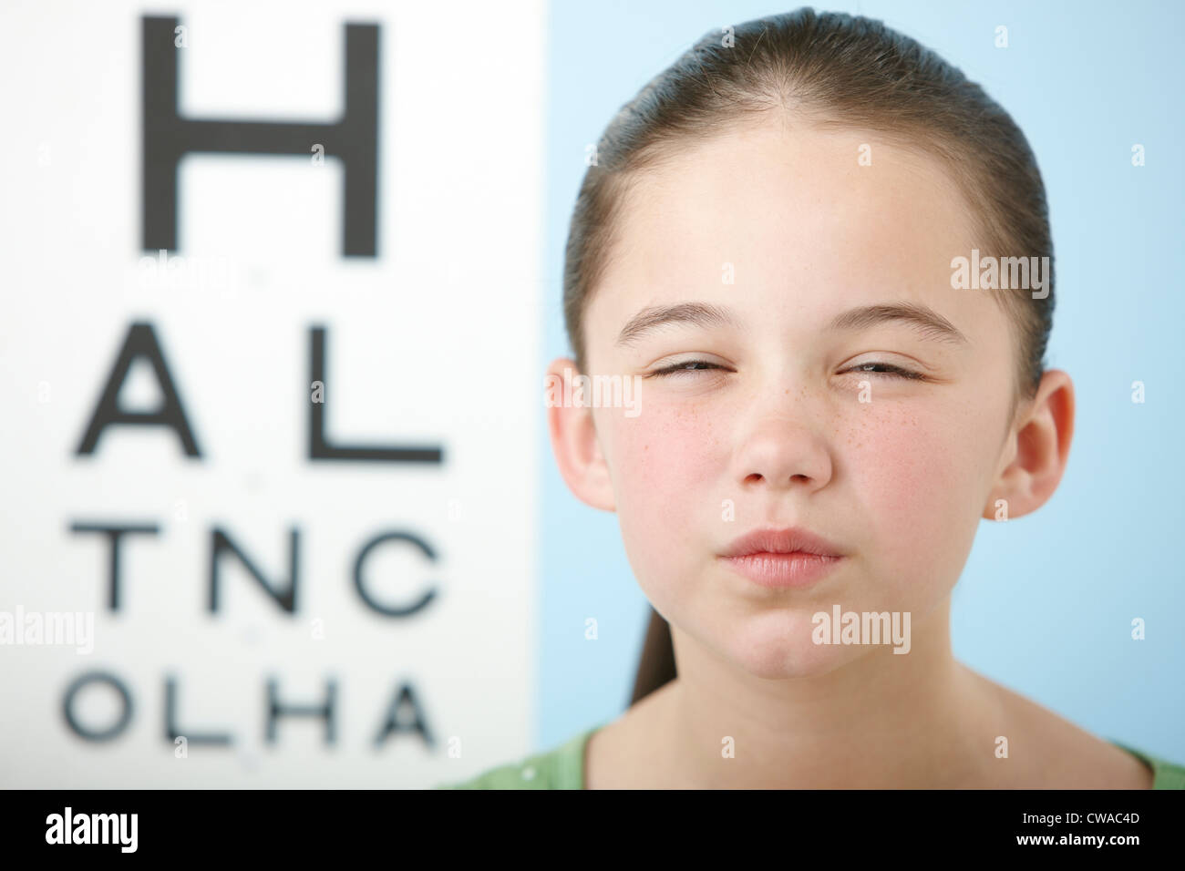 Girl squinting with eye chart in background Stock Photo - Alamy