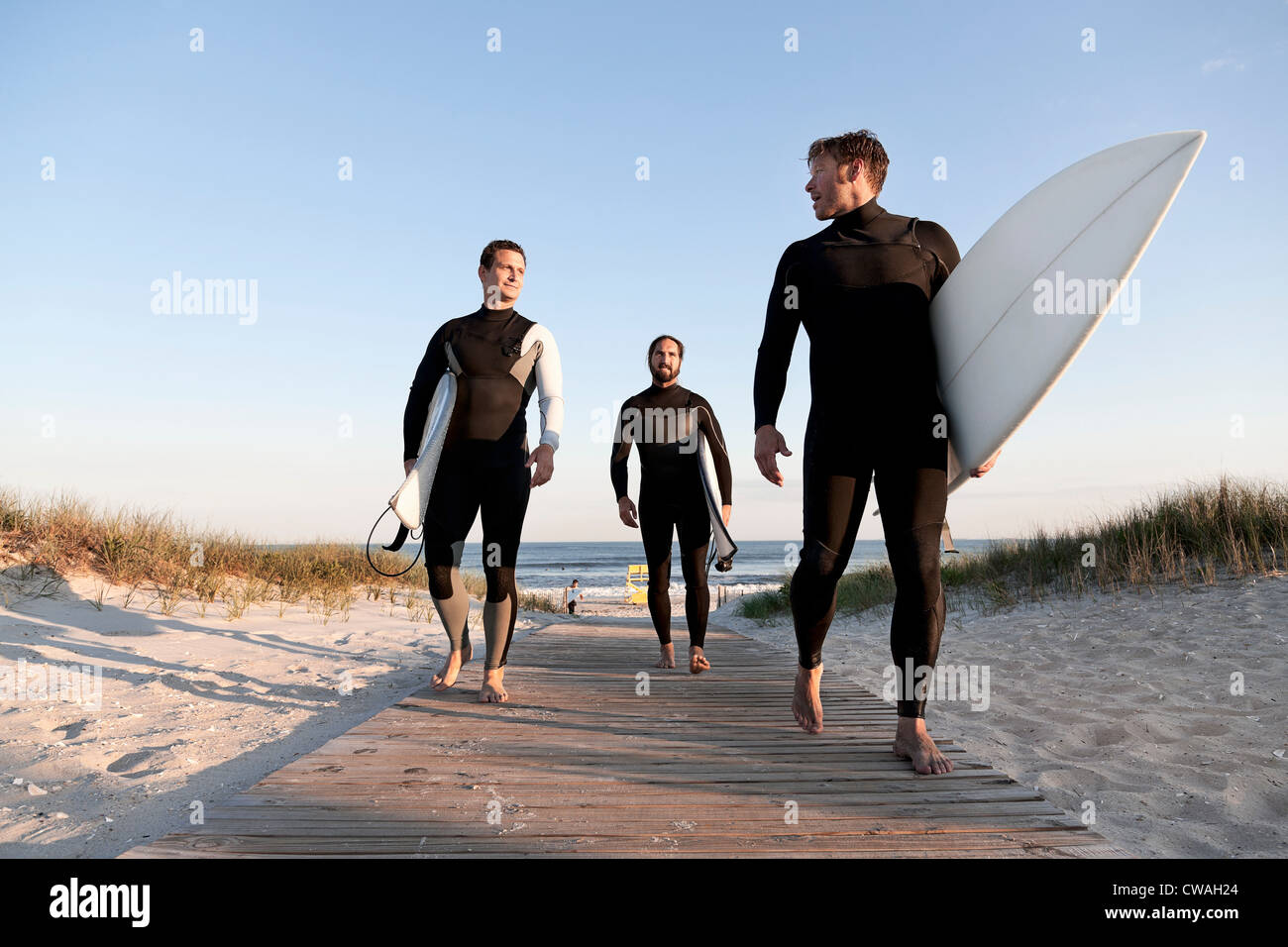 Three surfers walking on boardwalk Stock Photo - Alamy