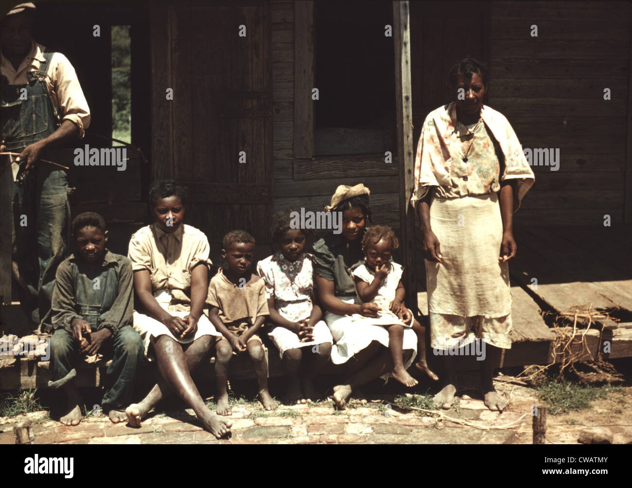 A rural African American family seated on the porch of their house on a ...