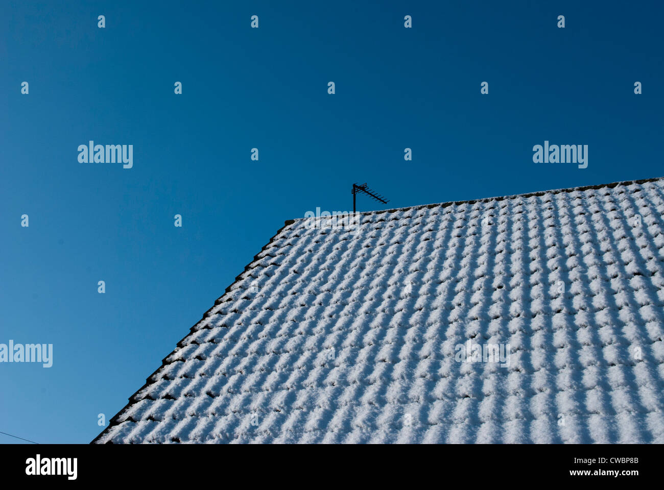 Snow covered tiled roof against a deep blue sky with television aerial ...