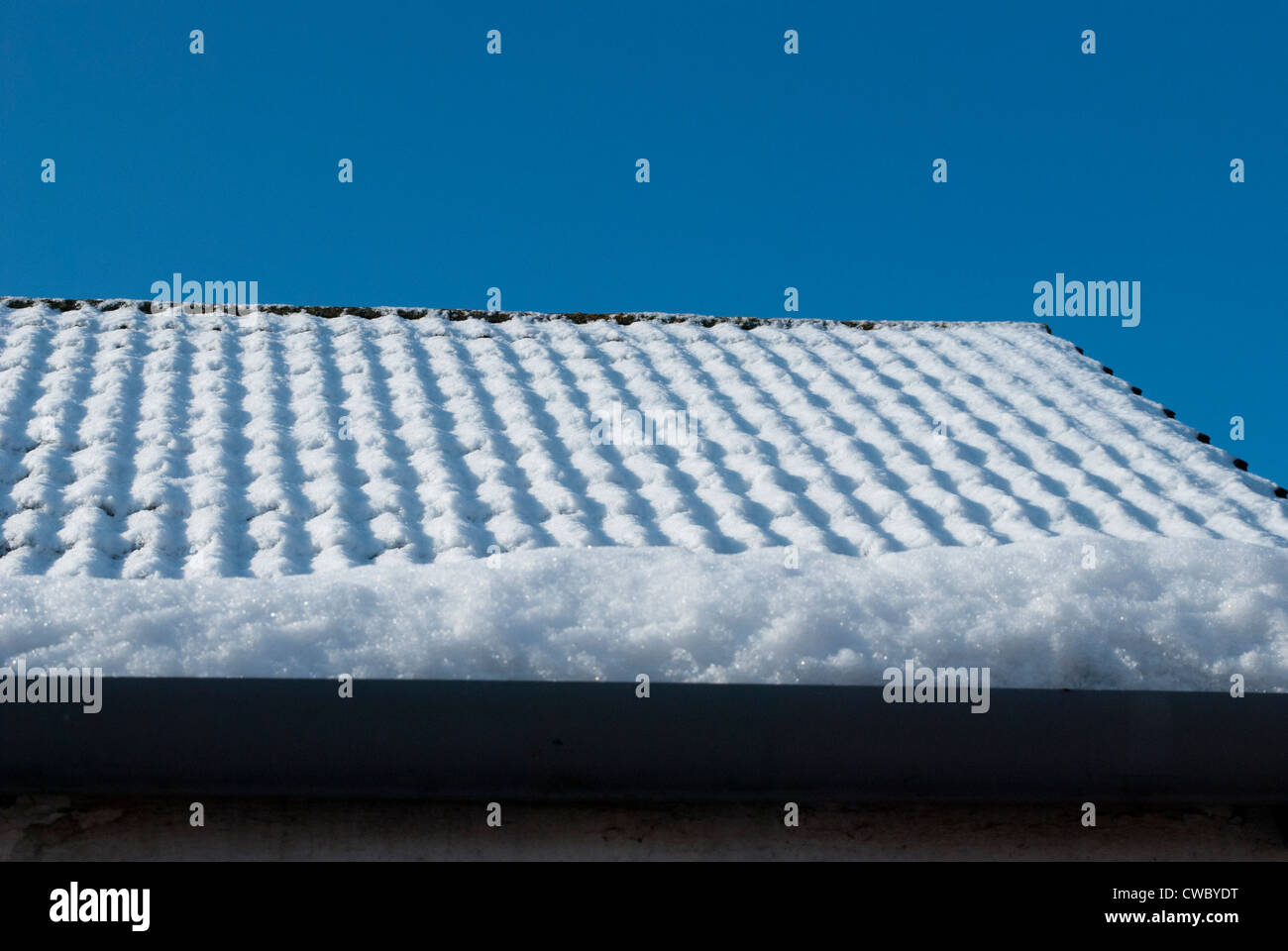 Snow covered tiled roof against a deep blue sky with snow filled ...