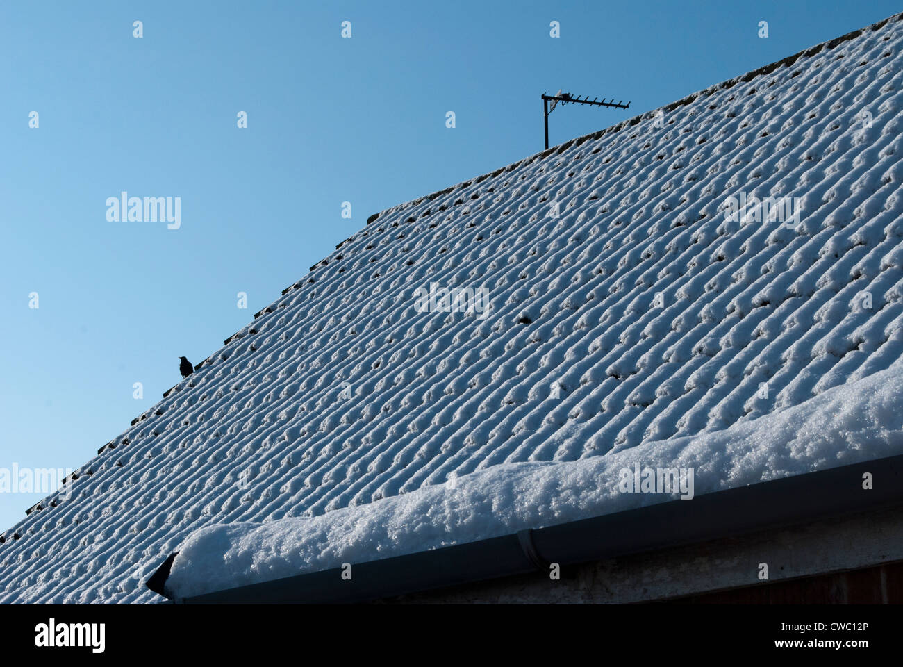 End of snow covered tiled roof against a deep blue sky with television ...