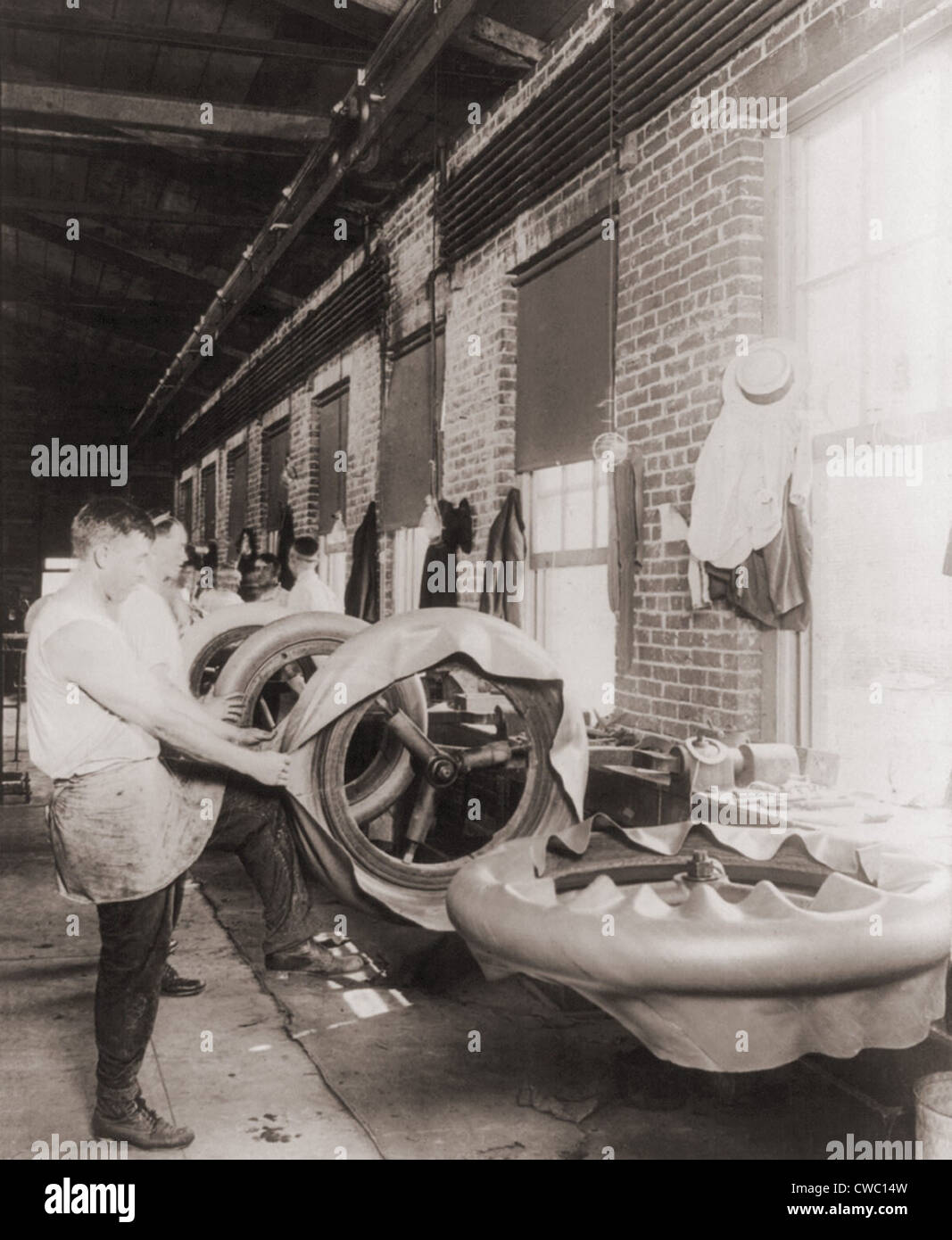 Workers in a tire shop applying the first ply of rubber on a handmade ...