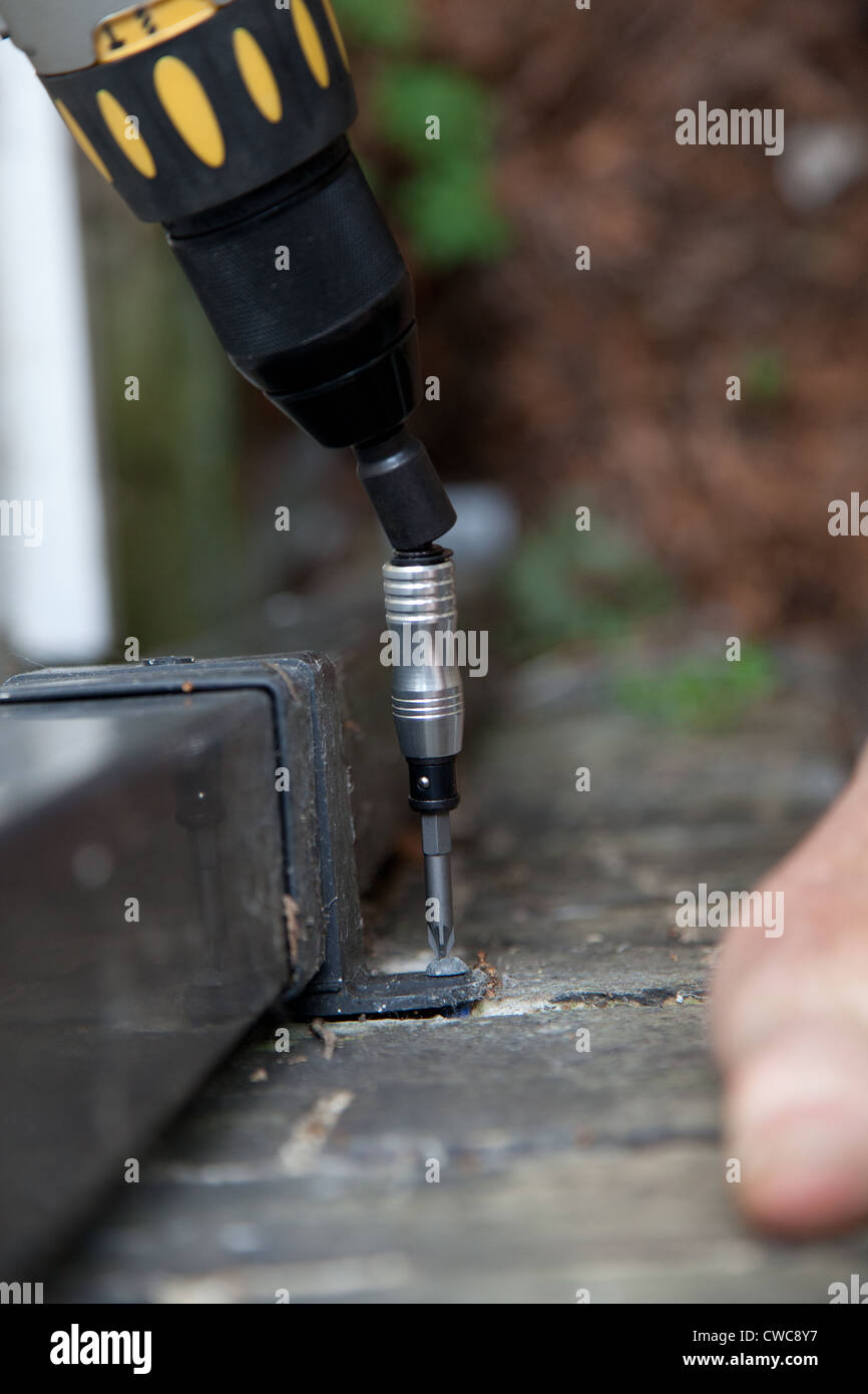 A man fixes a down pipe clasp with the help of an angled screwdriver ...