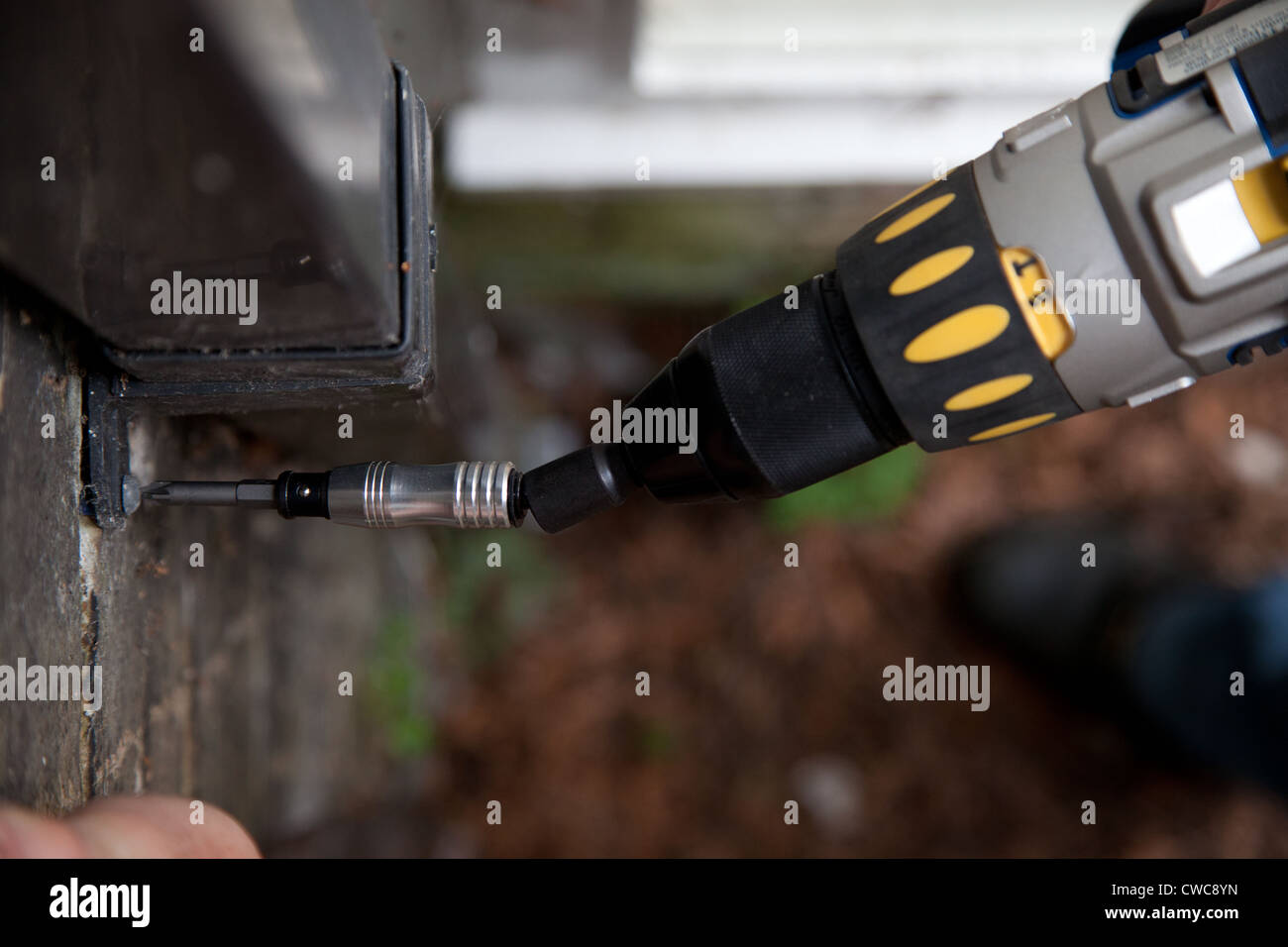 A man fixes a down pipe clasp with the help of an angled screwdriver ...