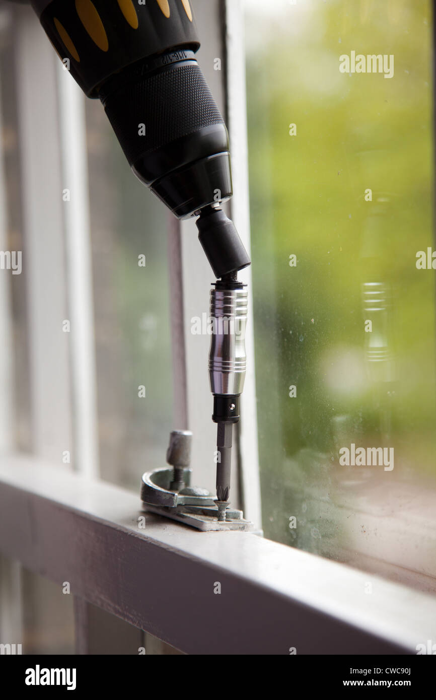 A man fixes a sash window clasp with the help of an angled screwdriver ...