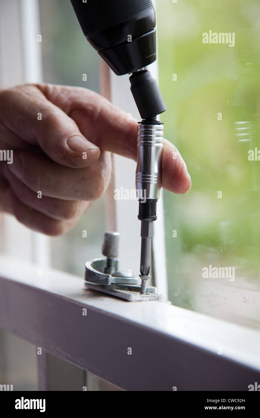 A man fixes a sash window clasp with the help of an angled screwdriver ...