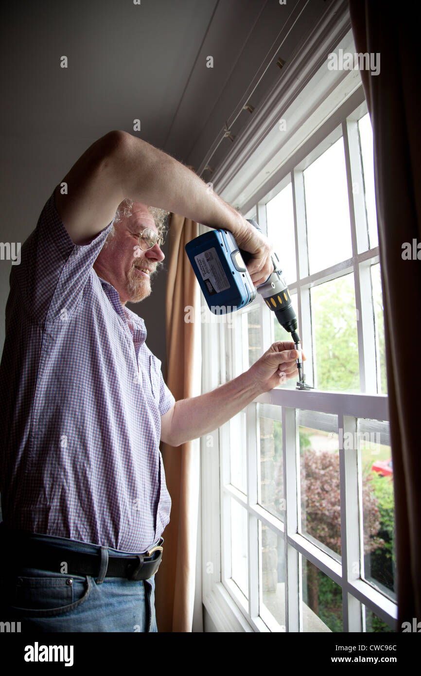 A man fixes a sash window clasp with the help of an angled screwdriver ...