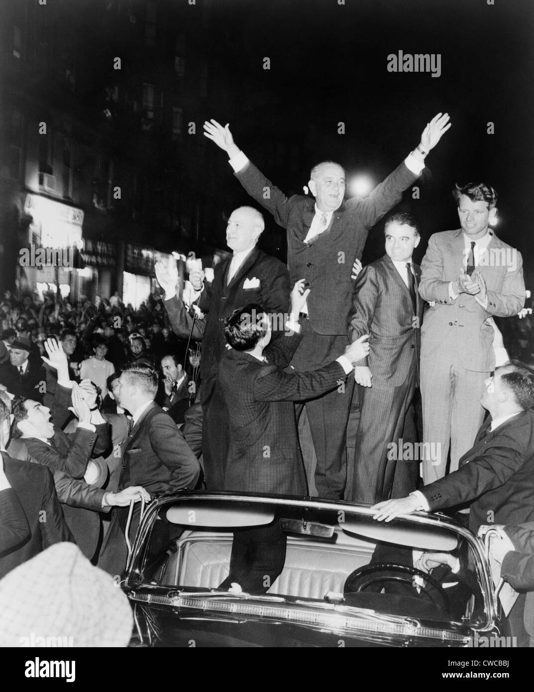 President Lyndon Johnson and Robert Kennedy standing on back of car ...