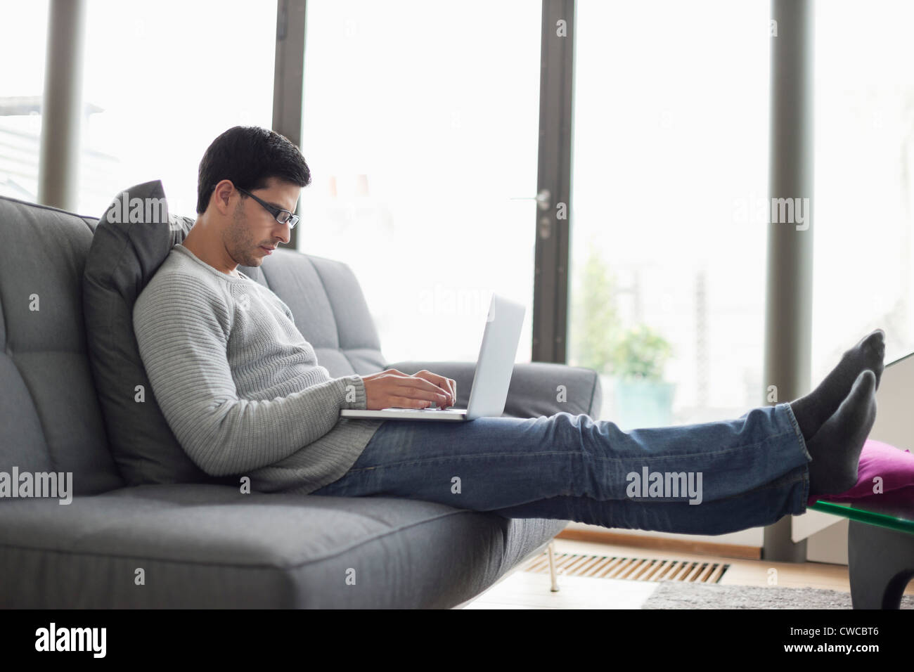 Man using a laptop on a couch Stock Photo - Alamy