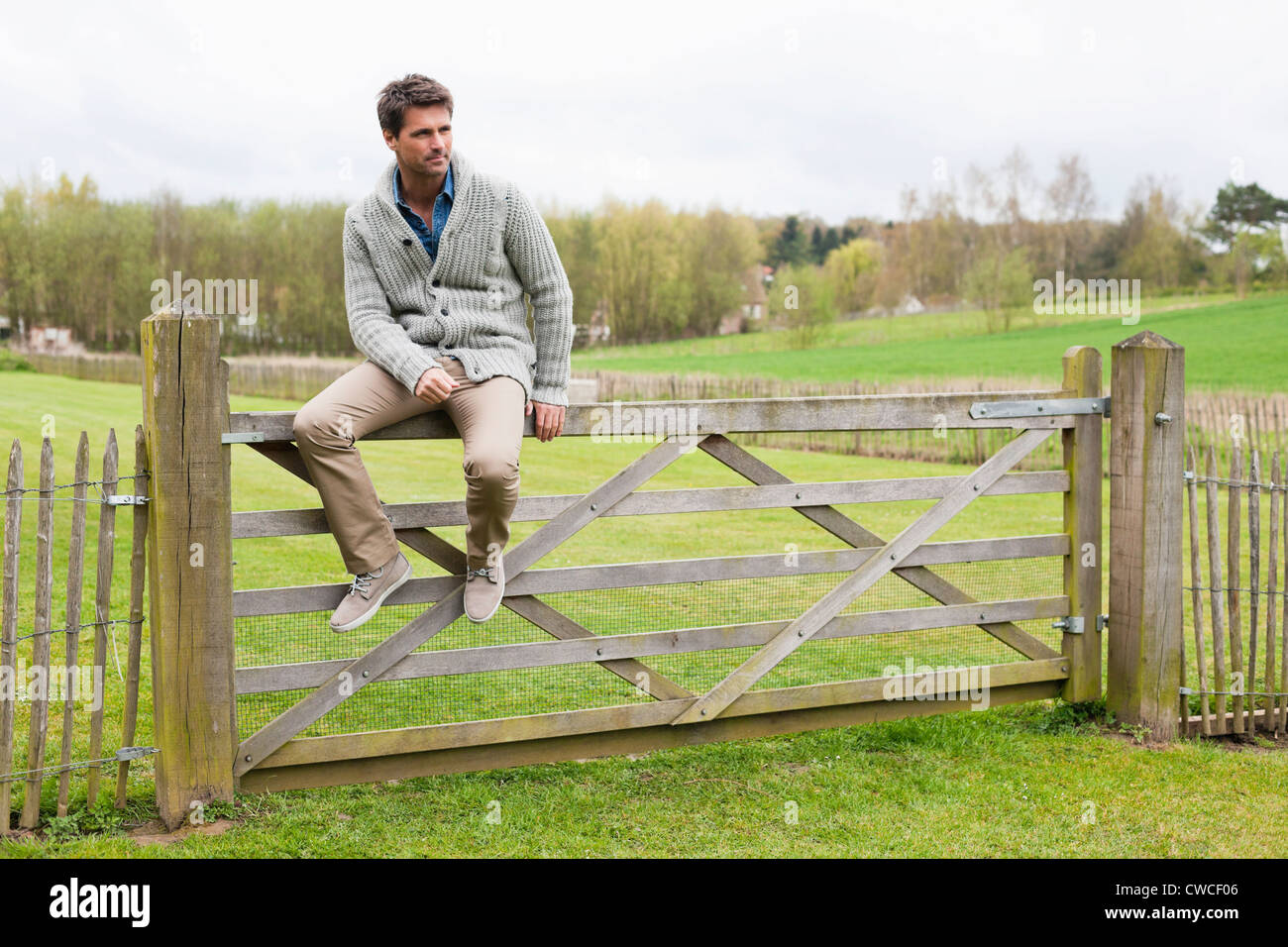 Man sitting on the gate of a cottage Stock Photo - Alamy