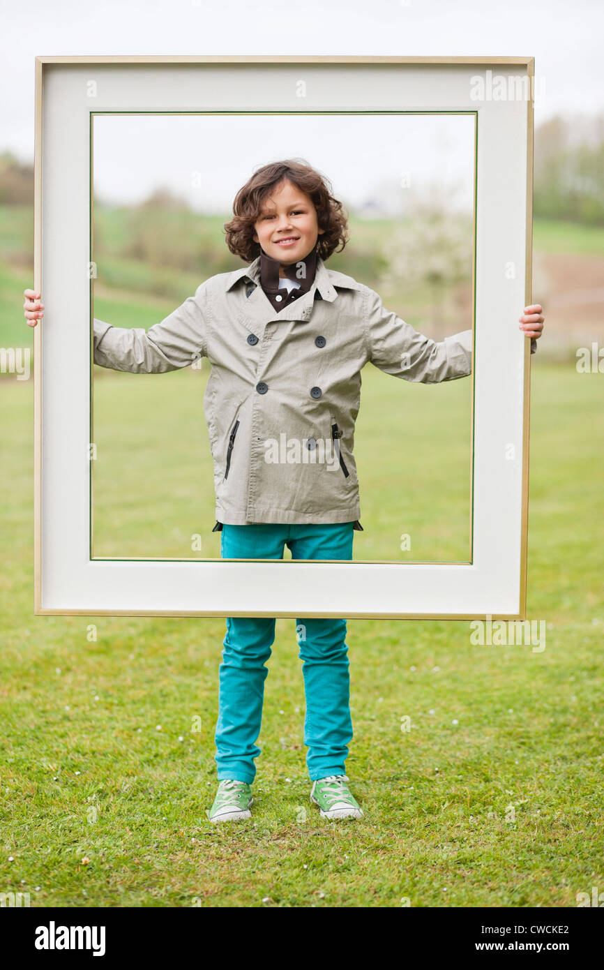 Portrait of a boy standing with a frame in a park Stock Photo - Alamy