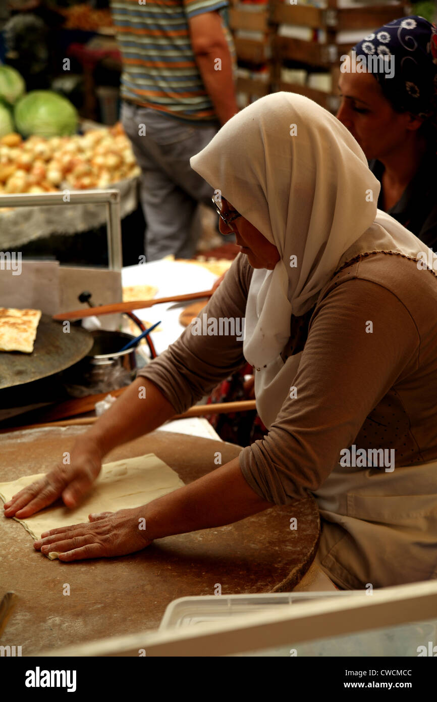 Woman wearing traditional headdress preparing Turkish bread in market ...