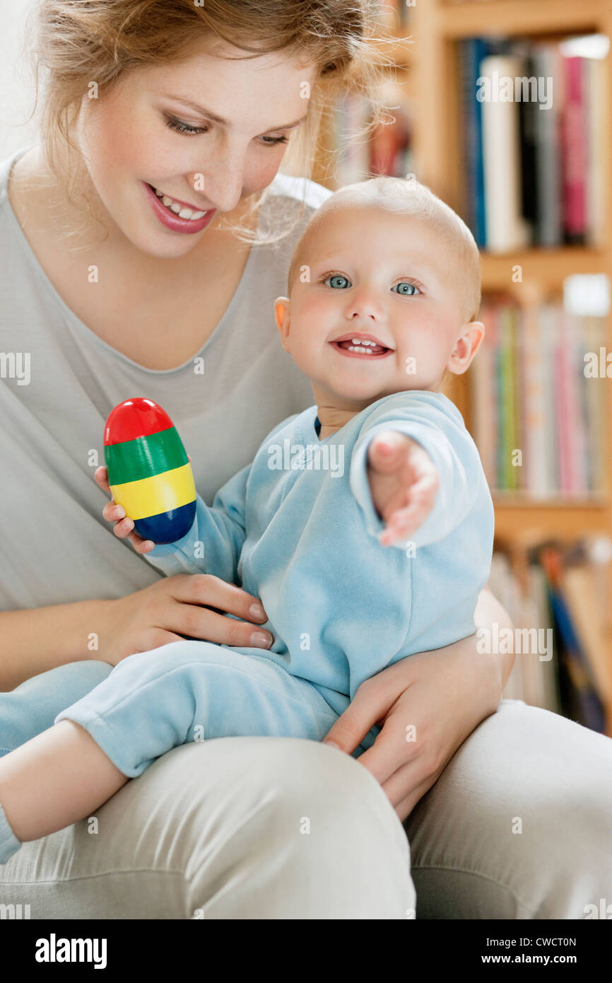 Baby girl sitting on the lap of her mother playing with a toy Stock ...