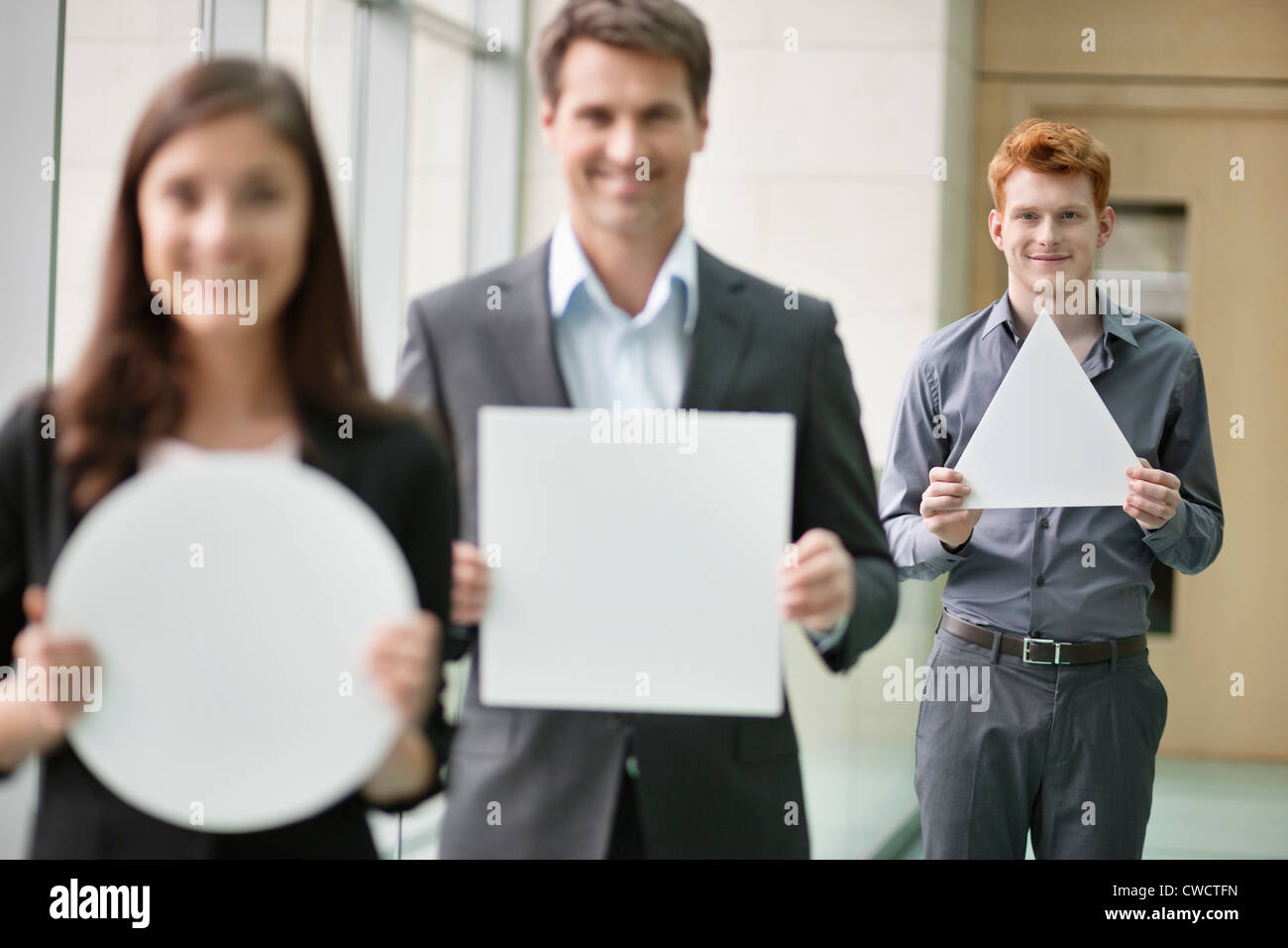 Business executives holding geometrical shaped placards in an office ...