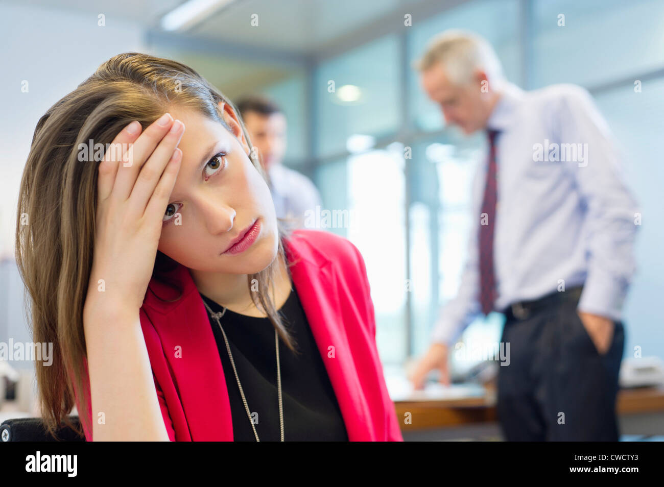 Female executive looking sad in an office with her colleagues ...