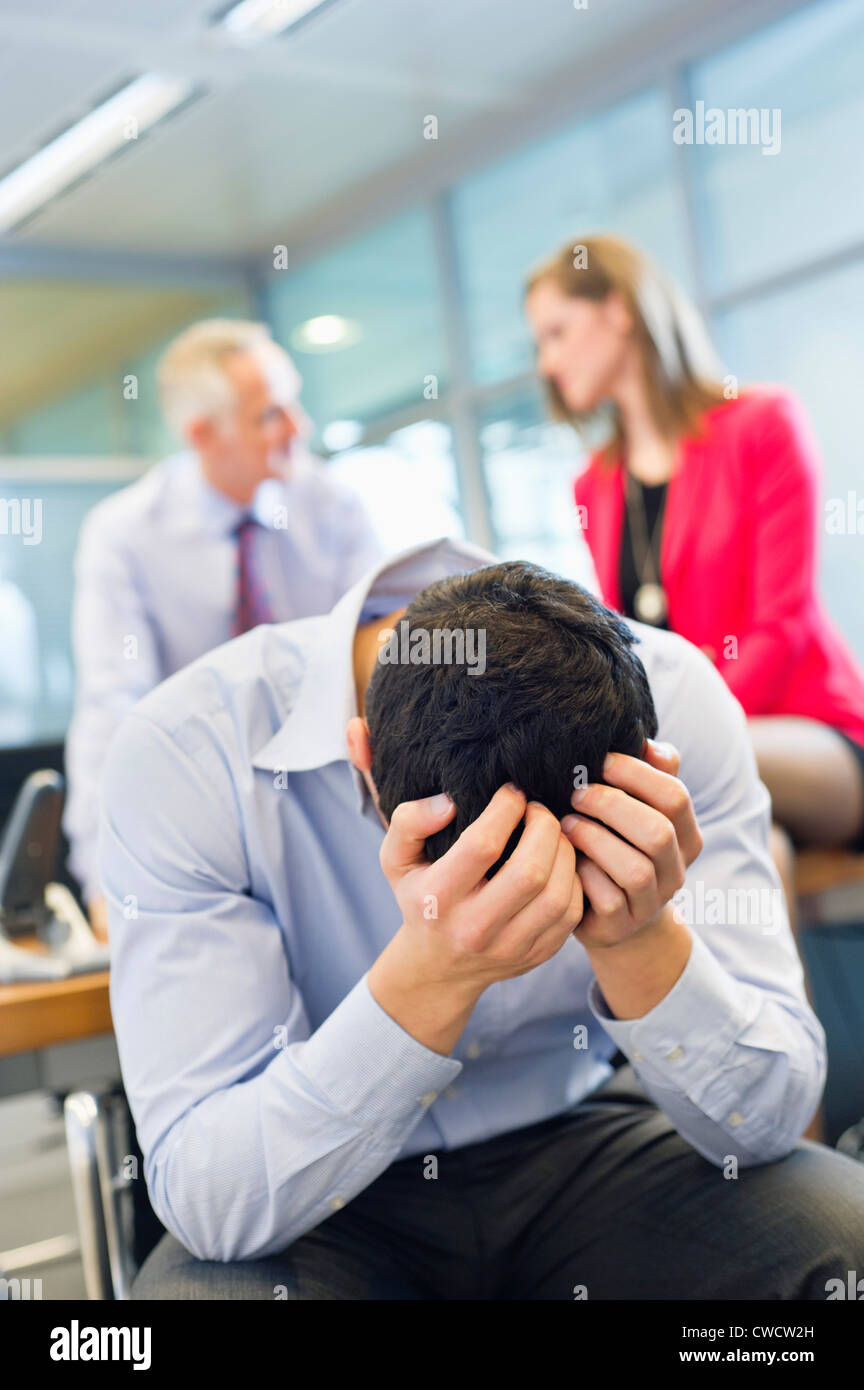Male executive looking worried in an office with his colleagues ...
