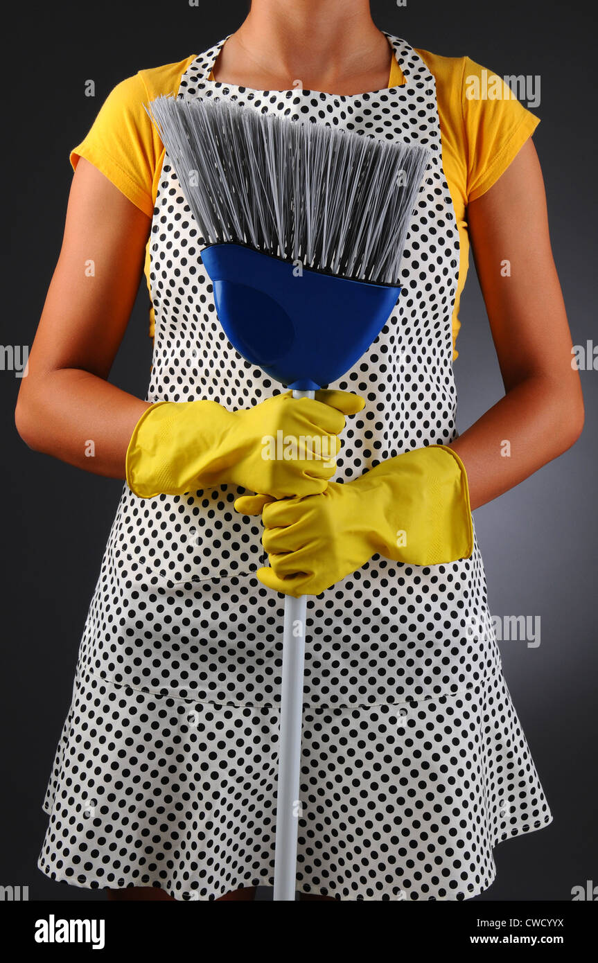 Closeup of a homemaker in an apron holding a broom in front of her ...