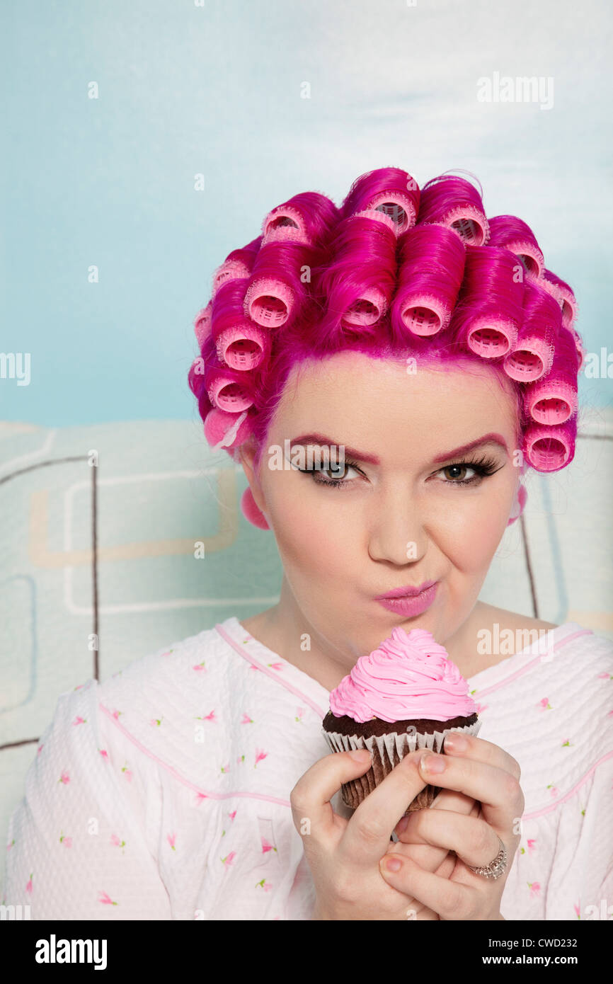 Portrait of a young woman making face while holding cupcake Stock Photo ...