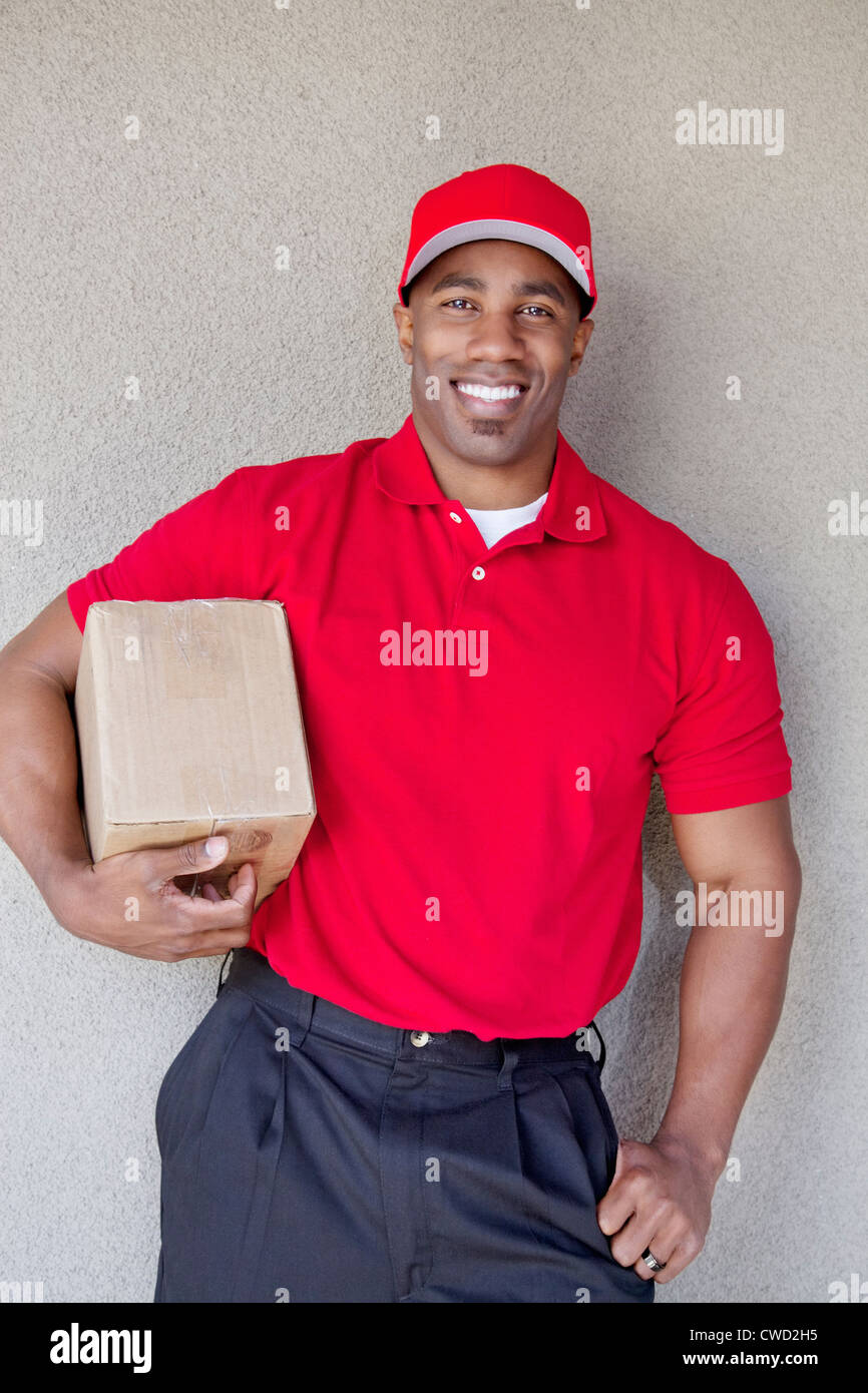 Portrait of a happy young man holding delivery box against wall Stock ...
