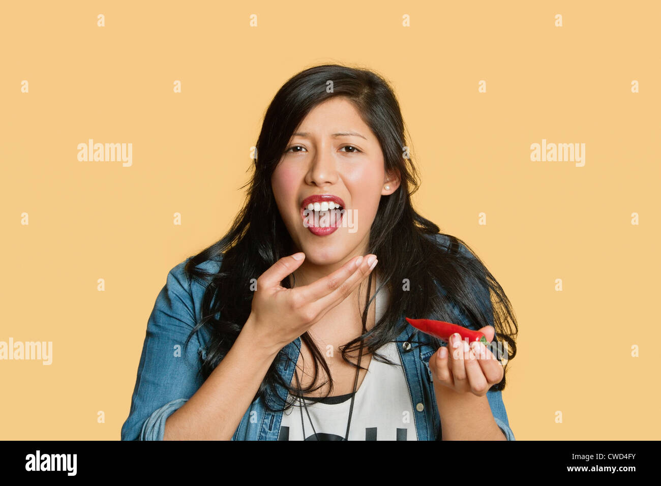 Portrait of a young woman eating red hot chili pepper over colored ...